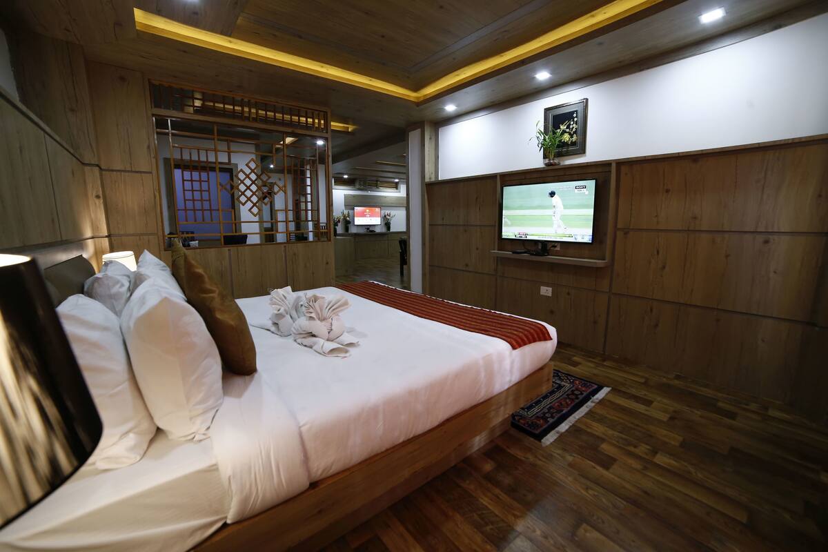 Quarto de hotel com cama de madeira, televisão fixada na parede e um ecrã decorativo tradicional.