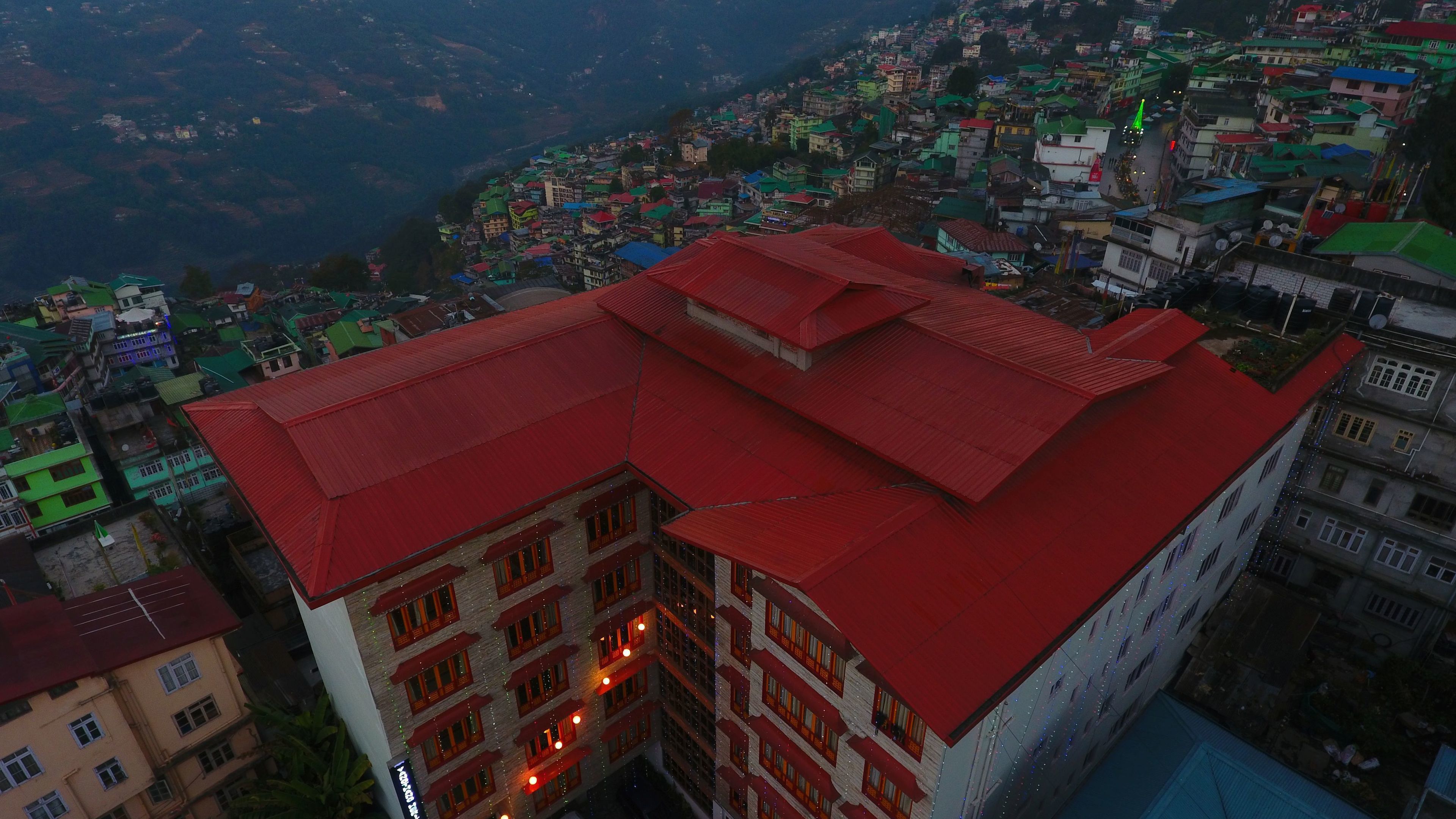 Um edifício de vários andares com telhado vermelho, cercado por outros edifícios com telhados verdes e vermelhos.