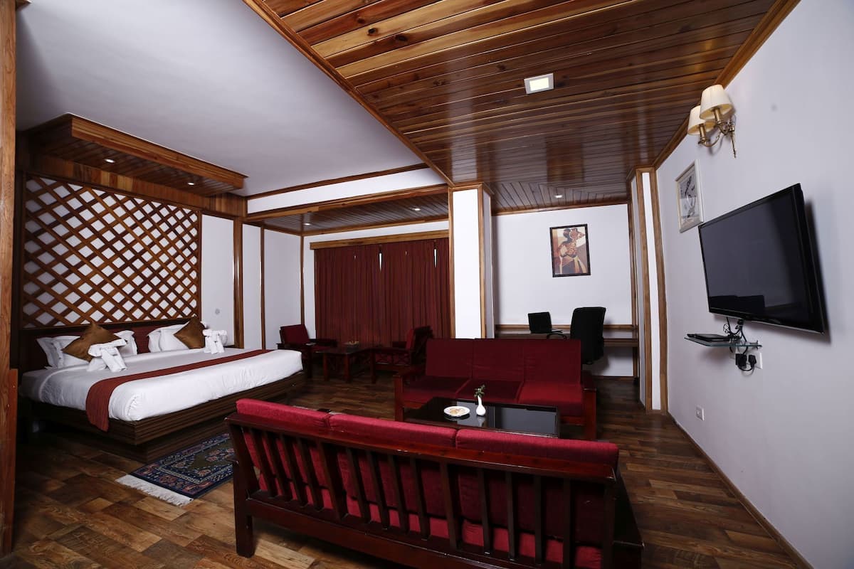 Quarto de hotel com uma cama, um sofá vermelho, uma televisão e teto de madeira.
