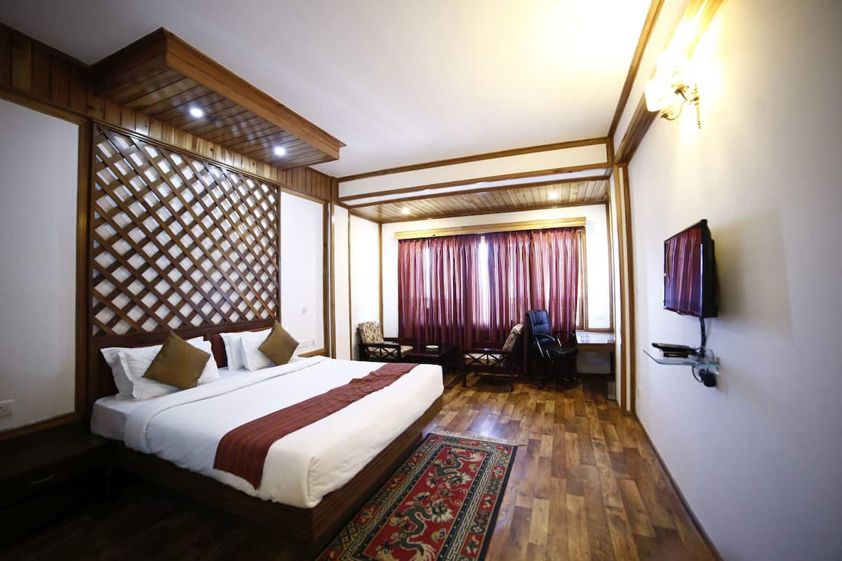 Quarto de hotel com uma cama grande, cabeceira de madeira, televisão fixada na parede e uma escrivaninha com cadeira.