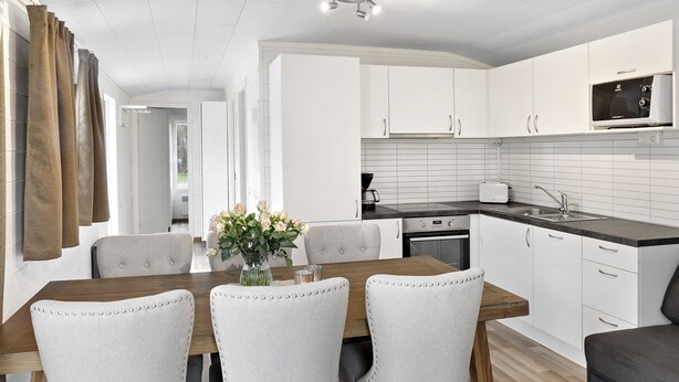 Cozinha moderna com armários brancos, micro-ondas e sala de jantar com mesa e cadeiras de madeira.