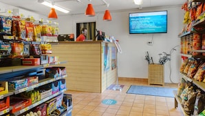 Interior de um supermercado com prateleiras cheias de lanches, um balcão de caixa e uma tela digital exibindo informações.