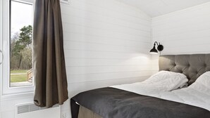 Um quarto com cama, janela com cortinas, luminária fixada na parede e radiador.