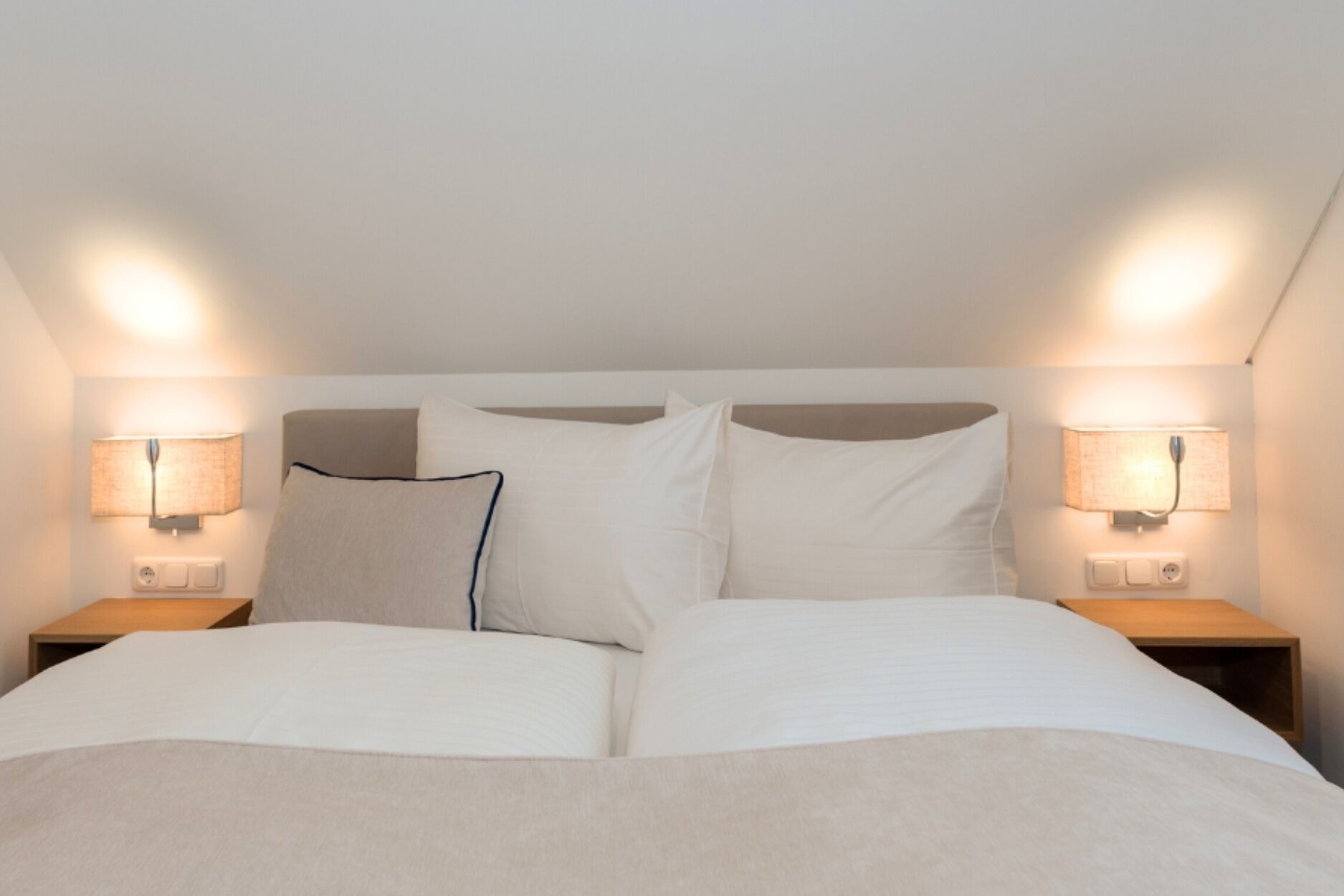 Uma cama de casal com lençóis brancos em um quarto com duas mesas de cabeceira, cada uma com uma luminária.