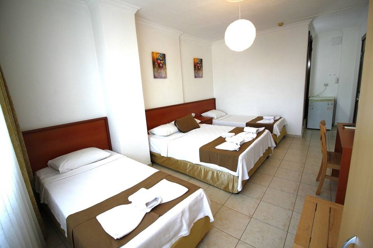 Quarto de hotel com quatro camas de solteiro, uma escrivaninha, uma cadeira e um frigorífico.