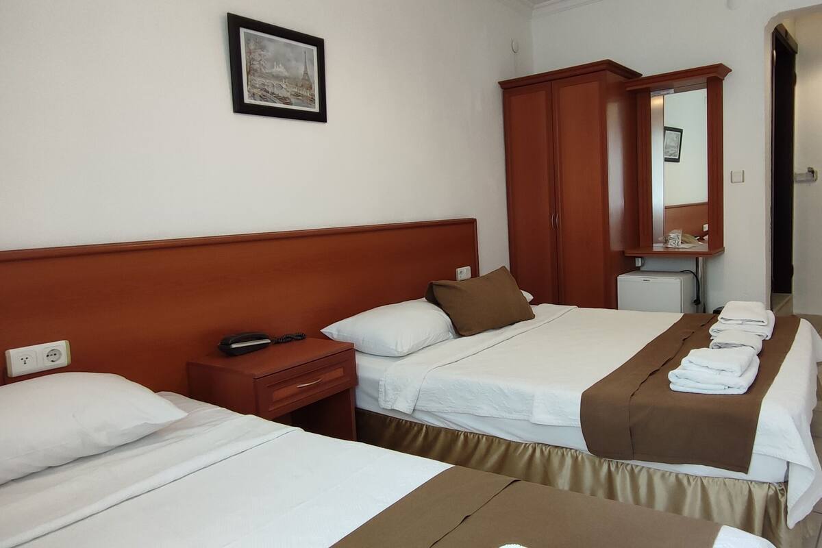 Quarto de hotel com duas camas, uma mesinha de cabeceira, um espelho e um quadro na parede.