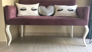 Um sofá roxo com pés brancos, decorado com almofadas estampadas com motivos de olhos e uma almofada em formato de coração.