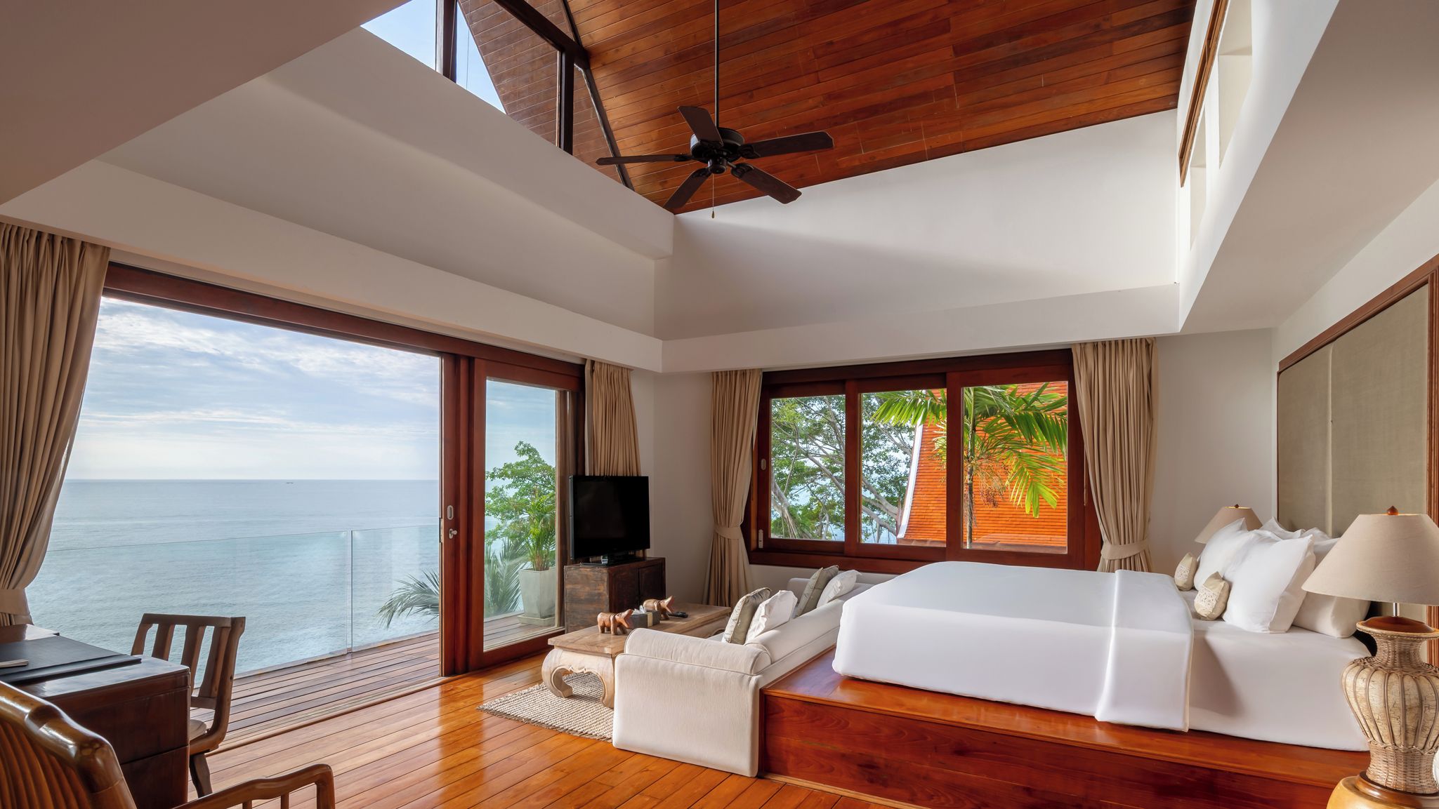 Quarto com uma cama grande, televisão e varanda vista para o mar.