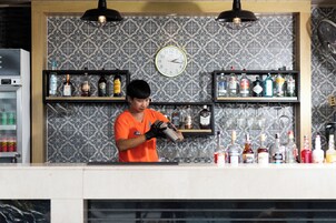 Uma área de bar com prateleiras de garrafas de bebidas, um relógio e uma pessoa preparando uma bebida.