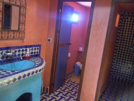 Casa de banho com lavatório azul, azulejos estampados e uma porta que dá para outro quarto.
