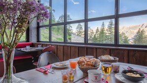 Mesa de café da manhã com ovos, torradas e suco, com vista para as montanhas.