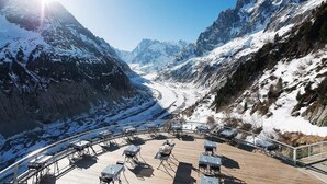 Um terraço com área de estar ao ar livre com vista para uma paisagem montanhosa nevada.