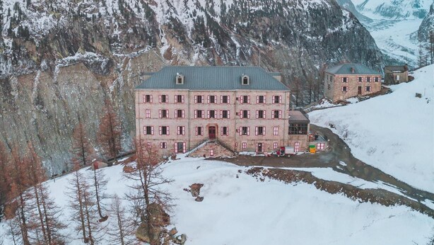 Um edifício grande e com vários andares, com fachada simétrica, situado numa área montanhosa coberta de neve.