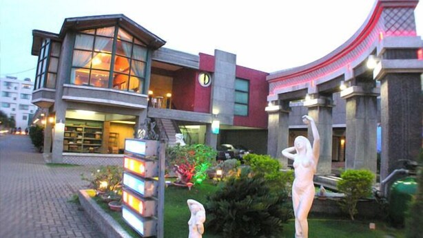 Um edifício moderno com fachada de vidro, esculturas ao ar livre e um jardim bem cuidado.