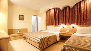 Quarto de hotel com duas camas, uma mesa de cabeceira com abajur, um criado-mudo com telefone e porta para o banheiro.