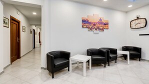 Uma área de recepção com cadeiras de couro preto, uma mesa branca e uma pintura com vista para a cidade na parede.