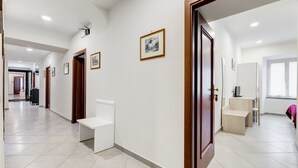 Um corredor amplo, com paredes brancas, portas de madeira e um banco.