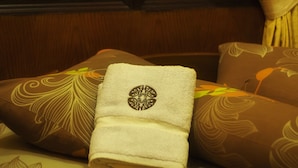 Uma cama com uma toalha branca dobrada e um travesseiro decorativo.