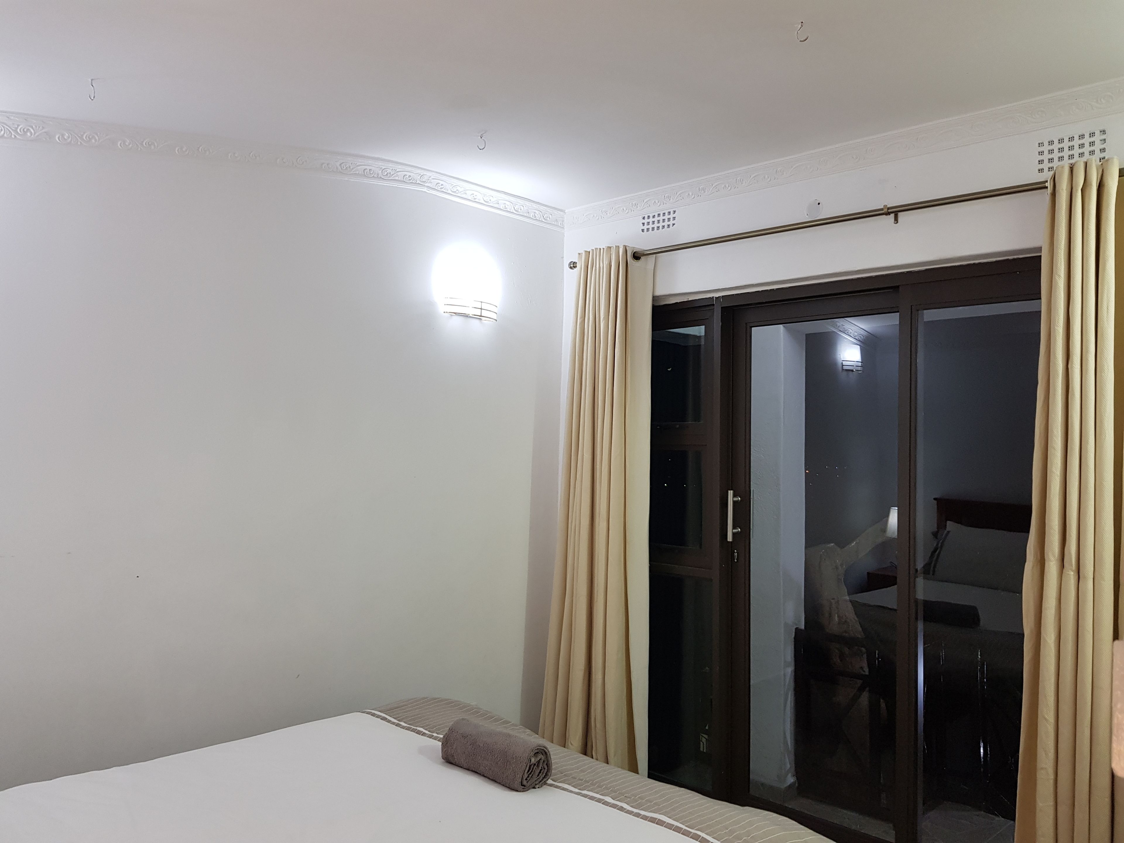 Quarto de hotel com uma cama, uma porta de vidro deslizante para uma varanda e uma pequena mesa com uma cadeira.