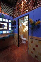 Casa de banho com parede azul, chão em mosaico, pia, sanita e janela com vista.