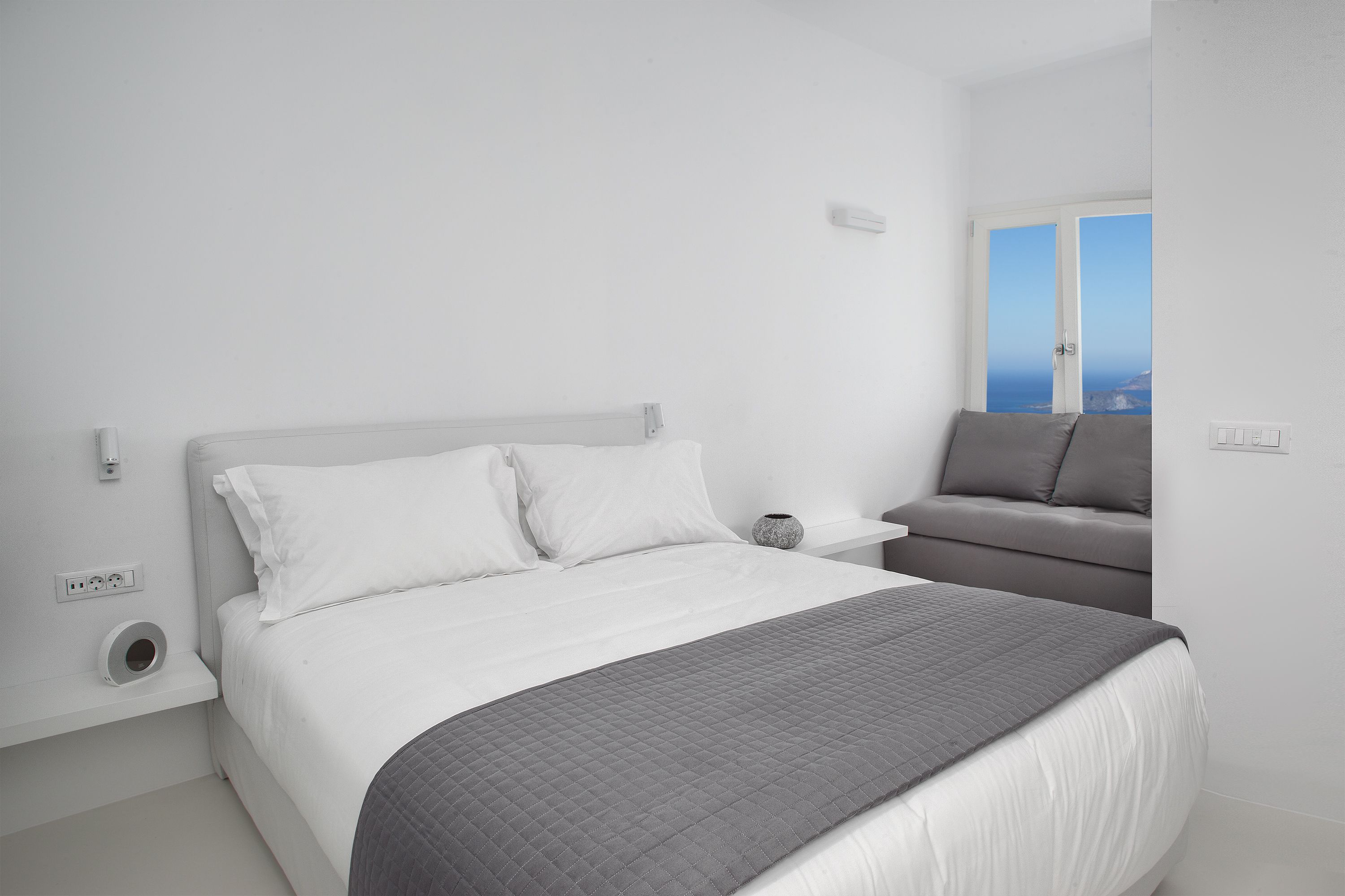 Quarto moderno com cama, mesa de cabeceira e vista para o mar pela janela.