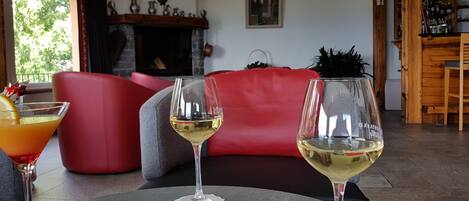 Um quarto com lareira, um sofá vermelho e duas taças de vinho sobre uma mesa.