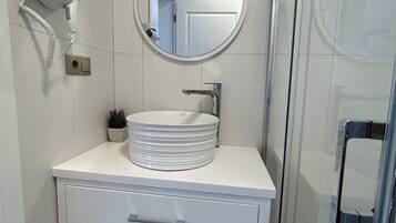 Uma casa de banho moderna com um espelho redondo, uma pia e um secador de cabelo fixado na parede.