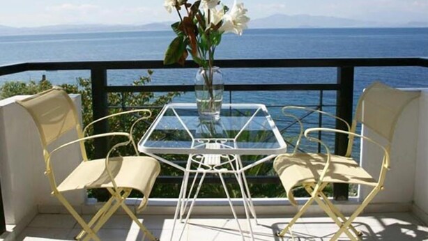Varanda com mesa de vidro e duas cadeiras, com vista para um corpo de água.