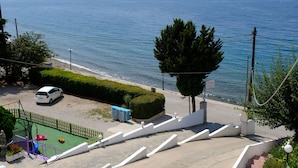 Área residencial com calçada pavimentada, um carro branco estacionado na rua e vista para o mar.