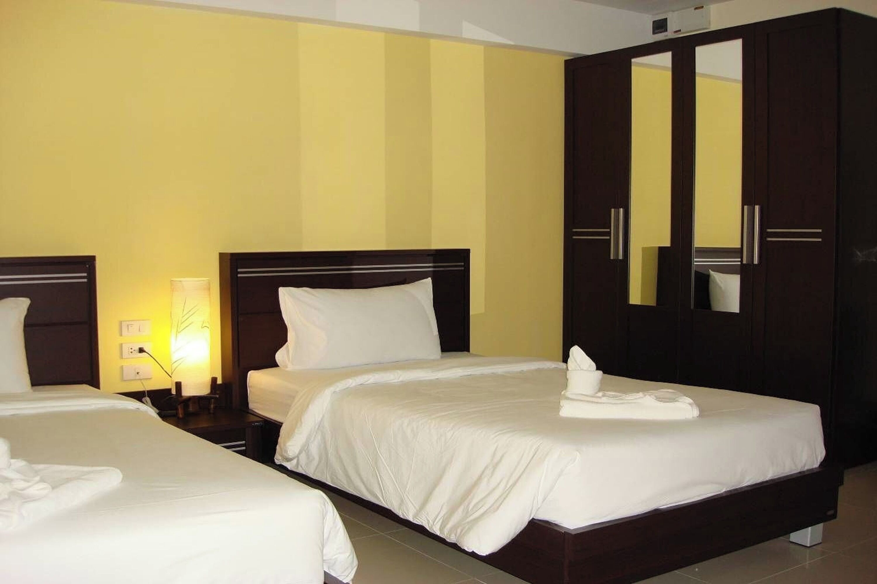 Quarto de hotel com duas camas, um guarda-roupa grande e uma mesa de cabeceira com uma luminária.