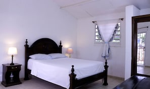 Uma cama de solteiro com cabeceira de madeira, duas mesas de cabeceira com abajures e uma janela com cortina.