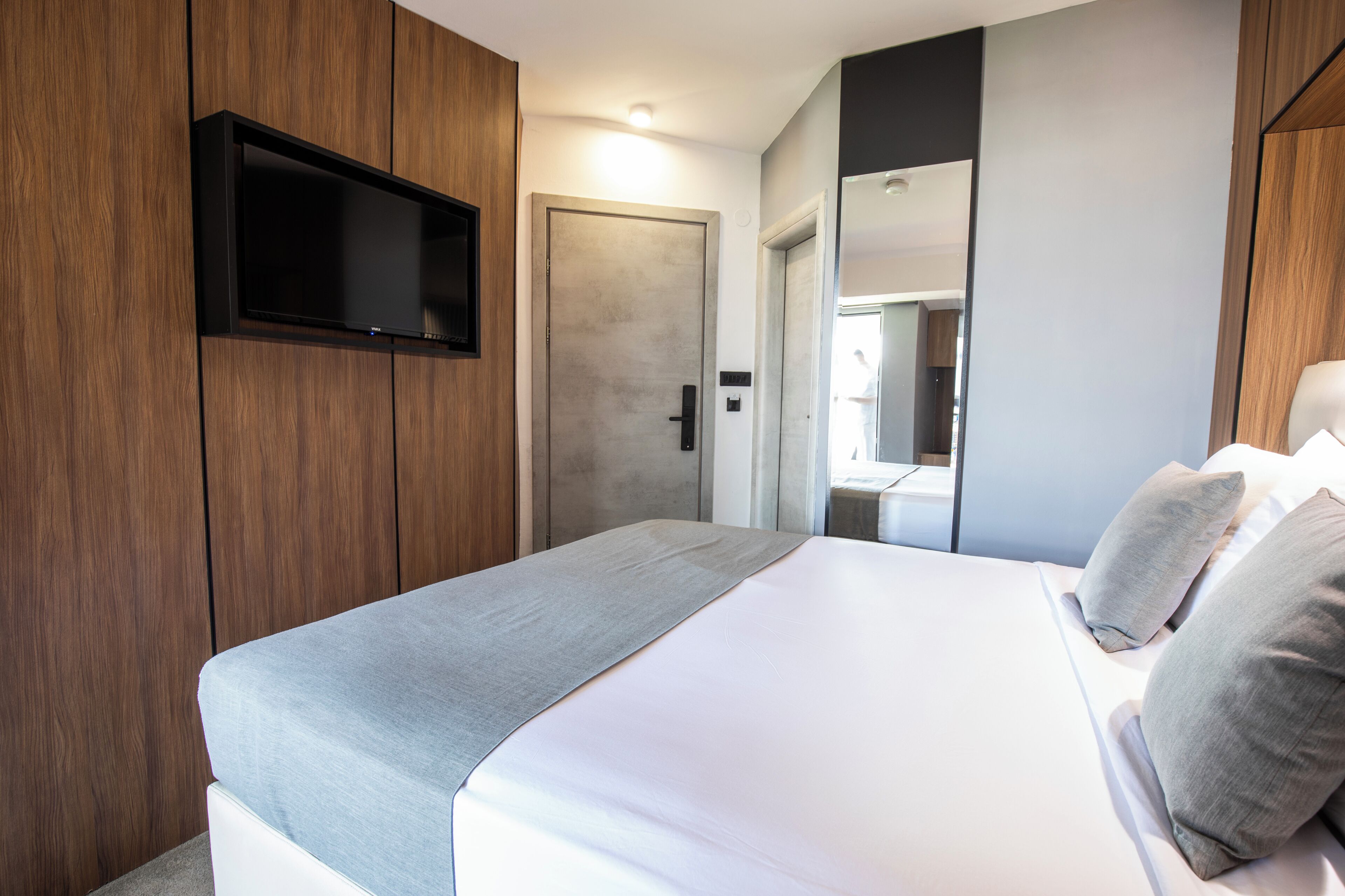 Quarto moderno com cama grande, guarda-roupa de madeira e televisão na parede.