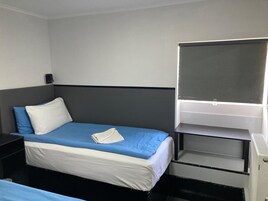 Quarto de hotel com uma cama, mesa de cabeceira, escrivaninha e uma janela.
