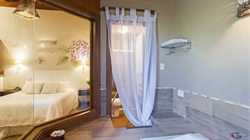 Quarto de hotel com uma cama grande, divisória de vidro, área de chuveiro e piso de madeira.