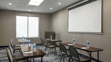 Sala de conferências com mesas, cadeiras, garrafas de água e uma tela de projeção.