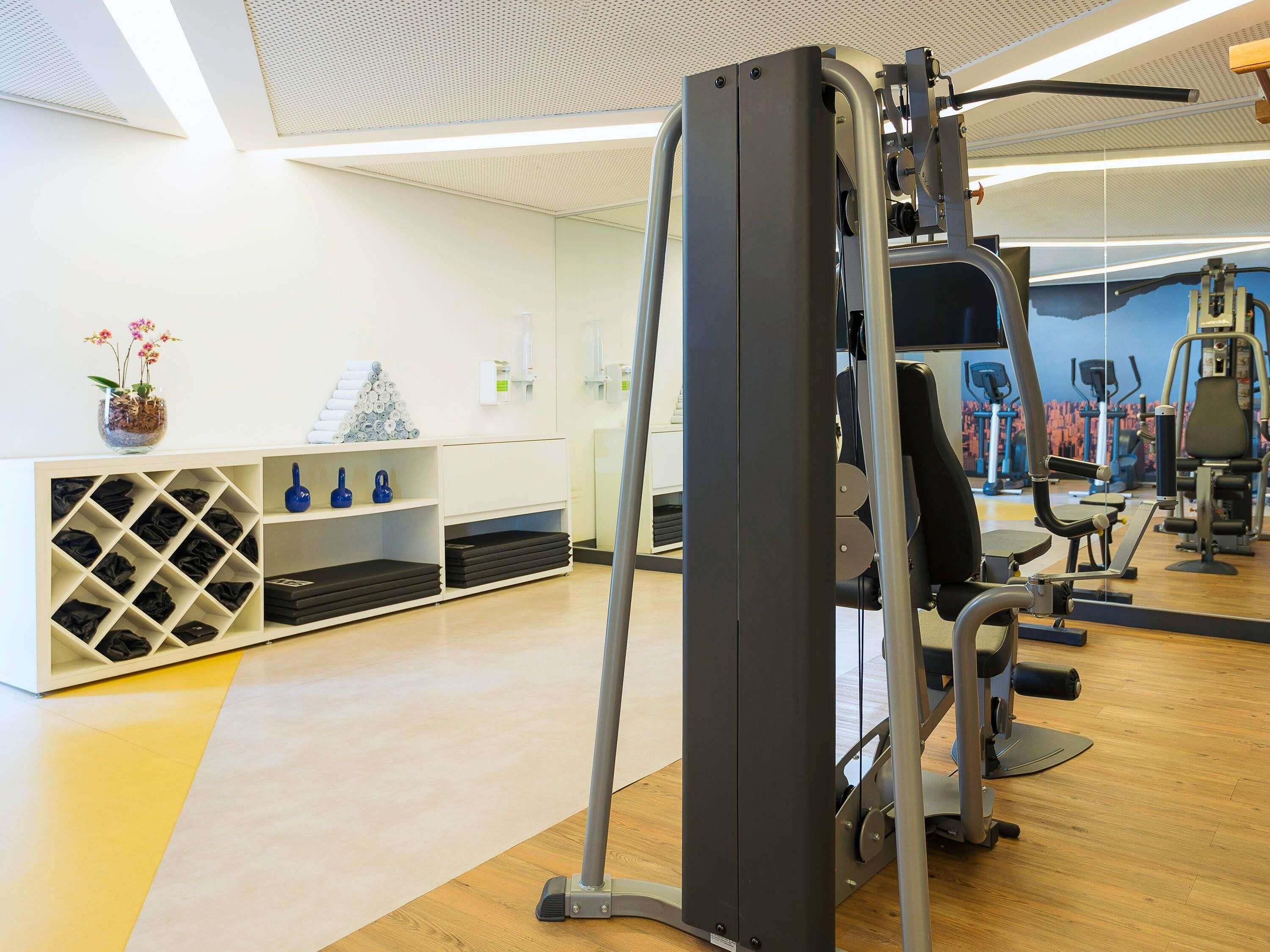 Uma academia com equipamentos de exercício, um balcão de recepção e uma prateleira com toalhas e um vaso.