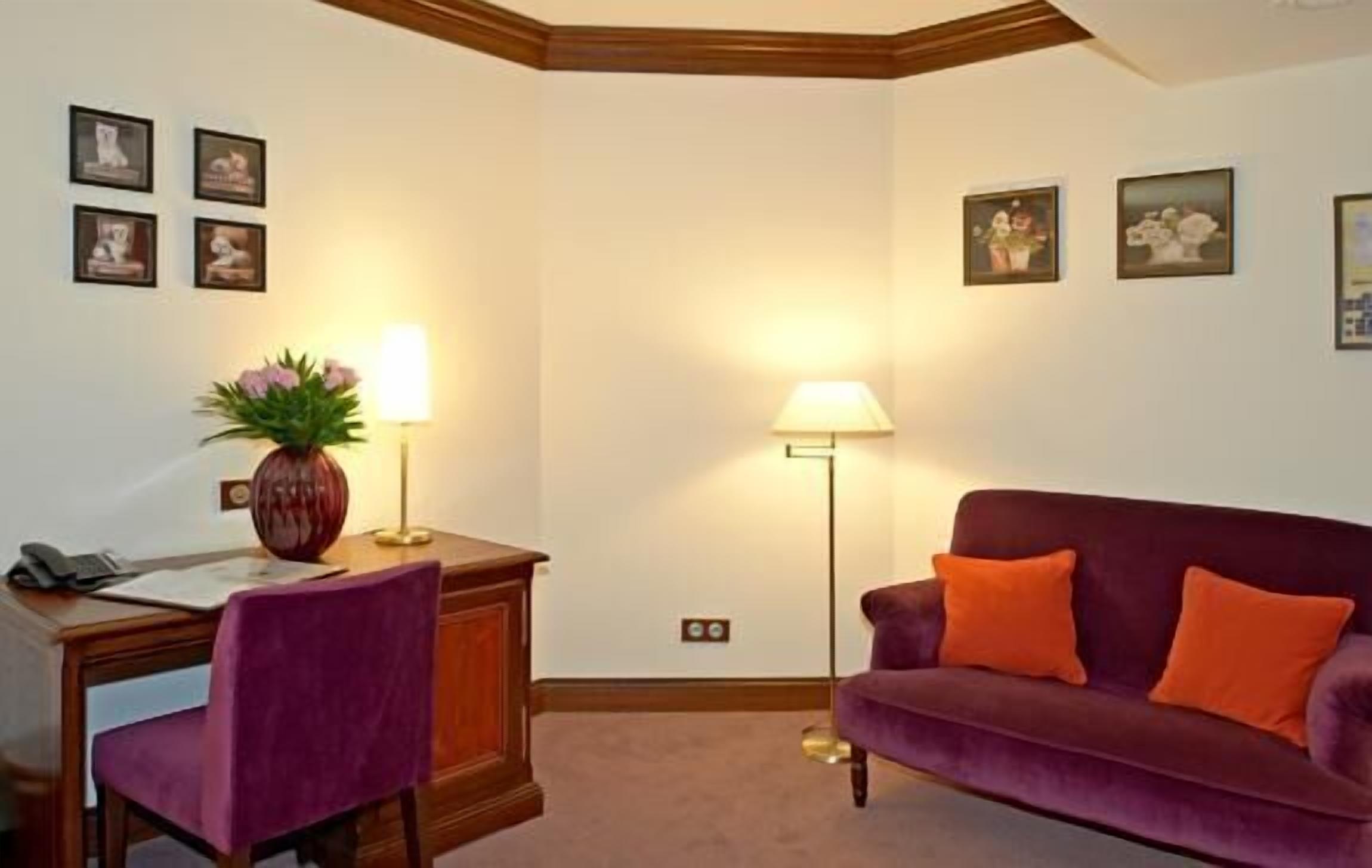 Um quarto com escrivaninha, poltrona roxa, sofá roxo e duas luminárias.
