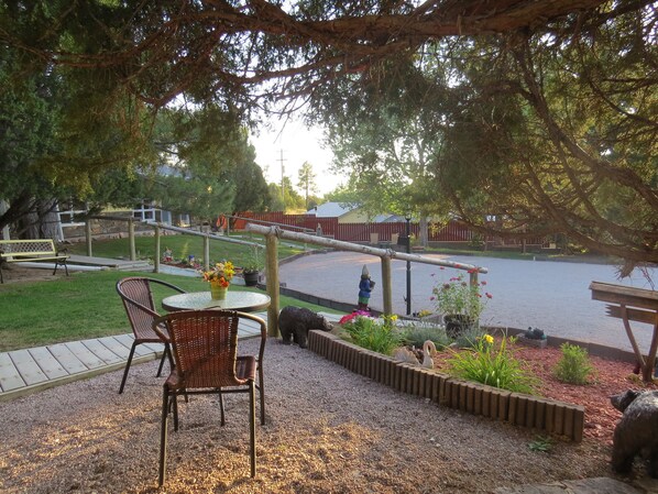 Um espaço de pátio com mesa e cadeiras, rodeado por um jardim com plantas e uma estátua decorativa de cisne.