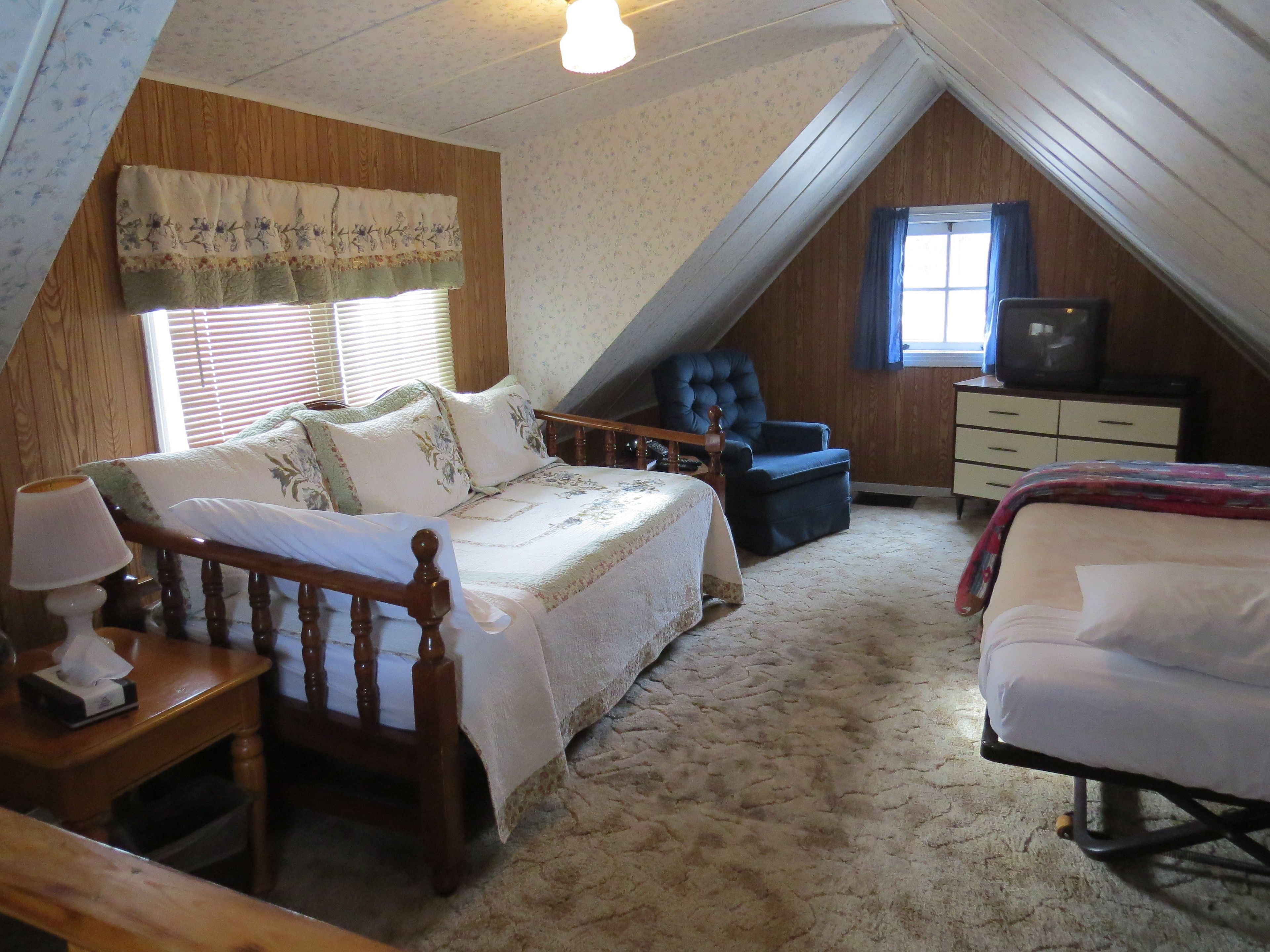 Quarto de sótão acolhedor com cama de madeira, uma cadeira, cômoda e televisão.