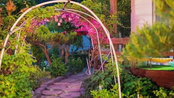 Uma trilha no jardim com um arco de madeira e uma pérgola florida em tons de rosa.