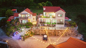 Uma casa de dois andares com um muro de pedra, uma varanda e um carro estacionado na frente.