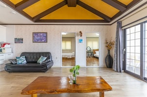 Uma sala de estar ampla com uma mesa de centro de madeira, um sofá de couro preto com almofadas estampadas, uma pintura emoldurada de paisagem urbana e uma janela grande com vista.