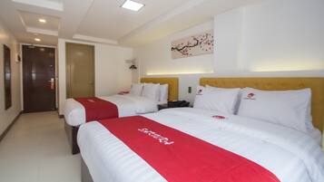 Quarto de hotel com duas camas, uma toalha vermelha, um relógio na parede e uma porta ao fundo.