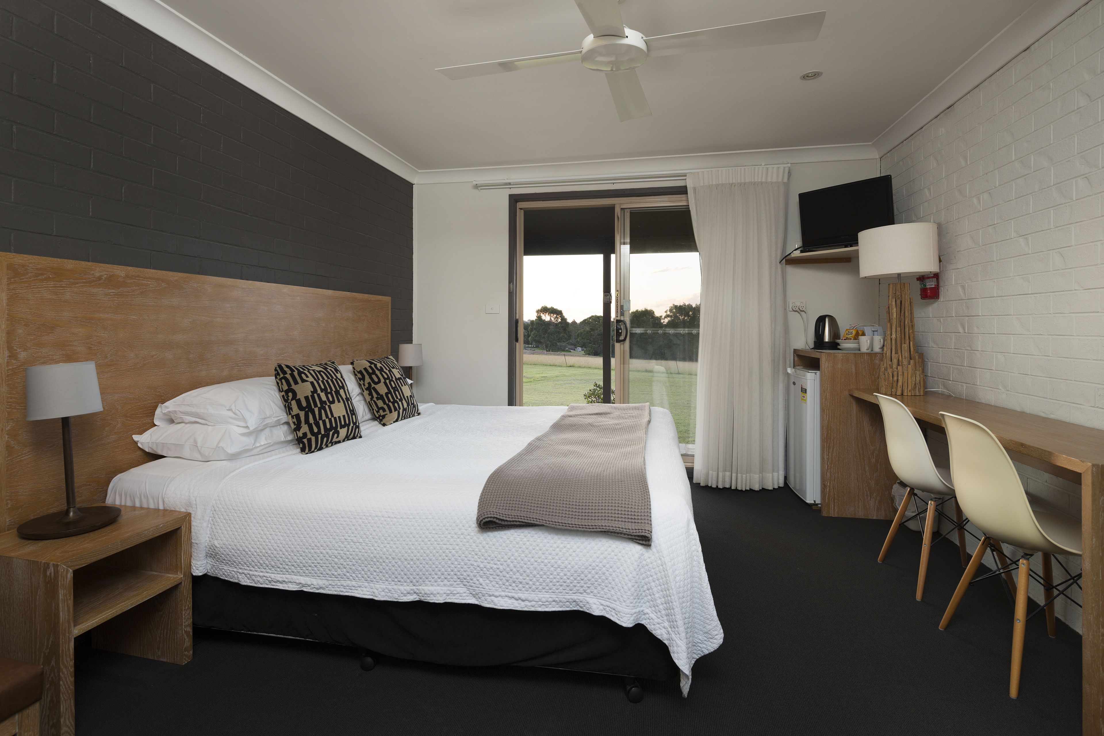 Quarto de hotel com uma cama grande, uma escrivaninha com cadeiras, uma televisão e vista para o exterior.