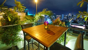 Mesa de madeira com uma vela e um enfeite de vidro numa varanda com vista para uma paisagem urbana à noite.