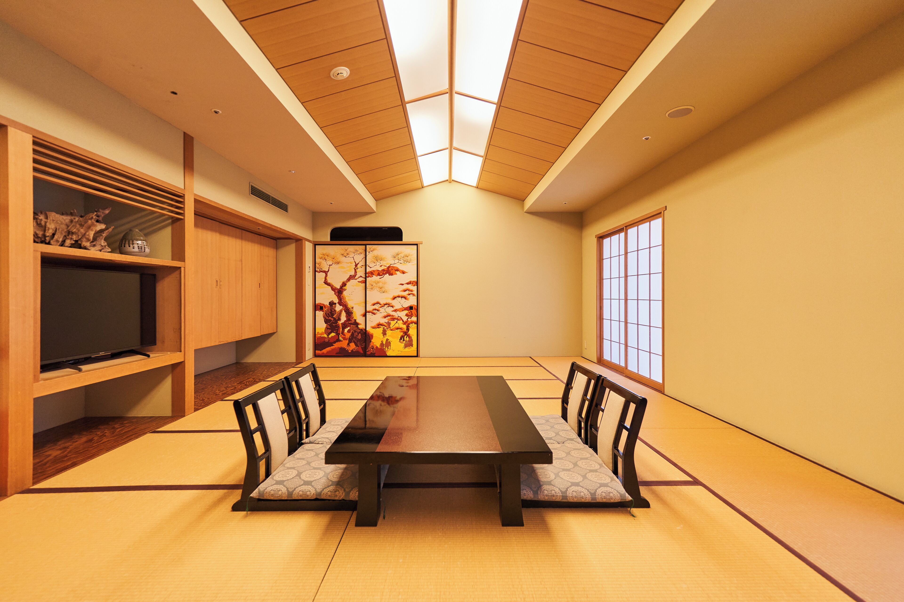 Um quarto em estilo japonês tradicional, com tatames, uma mesa baixa e almofadas, e uma televisão numa prateleira.