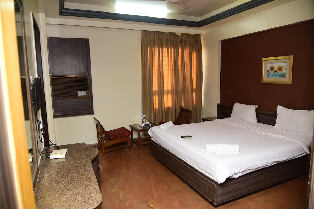 Quarto de hotel com uma cama grande, uma escrivaninha com cadeira, uma mesinha com um frasco e um quadro na parede.