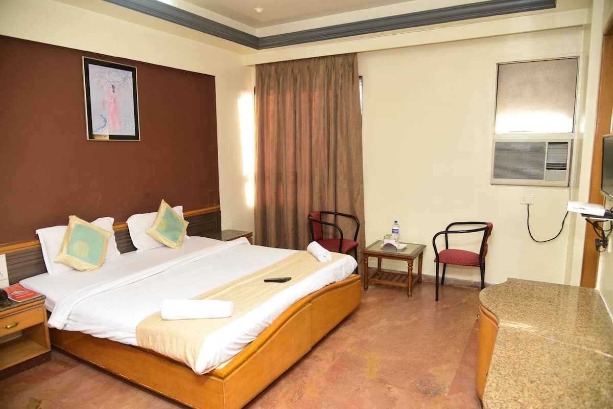 Quarto de hotel com uma cama grande, uma escrivaninha, uma cadeira e uma televisão.