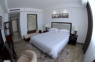 Quarto de hotel com uma cama grande, duas mesas de cabeceira, um sofá, uma cadeira e um quadro na parede.