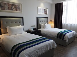 Quarto de hotel com duas camas, uma mesa de cabeceira com telefone e uma luminária.
